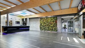 Um hall espaçoso com balcão de atendimento, parede coberta de vegetação e um restaurante chamado 'RESTAURANCE BOWLING'.
