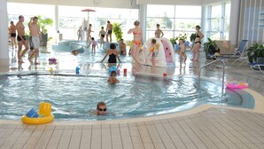 Piscina interior com várias pessoas, incluindo crianças e adultos, nadando e brincando.
