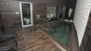 Uma área interna de piscina moderna, com piso de madeira escura, guarda-corpos de vidro e uma porta que dá para outro espaço.