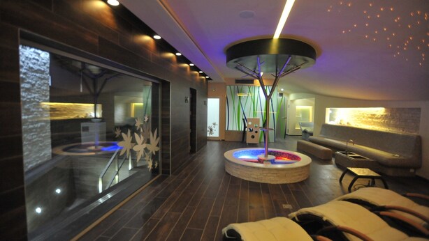 Uma área de spa moderna, com piso aquecido, um elemento central de água e uma área de estar com cadeiras de massagem.