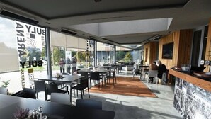 Um restaurante moderno com janelas amplas, mesas pretas e um painel de parede em madeira.