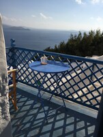 Varanda com mesa e cadeira, com vista para um corpo de água e terra ao longe.