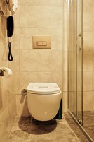 Casa de banho com sanita, cabine de chuveiro em vidro, telefone e interruptor de luz na parede.