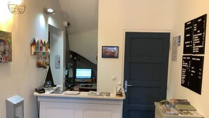 Balcão de recepção com computador, uma porta e parede com lista de tipos de quarto e preços.