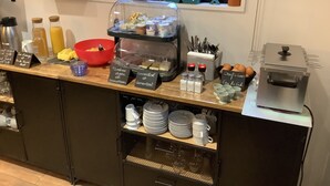 Uma mesa de pequeno-almoço com diversos alimentos, acompanhamentos e utensílios.