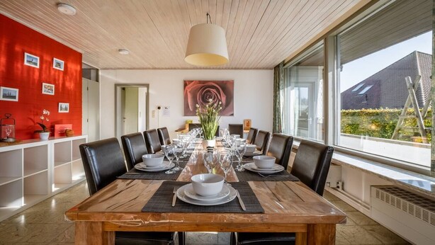 Uma sala de jantar moderna com uma mesa de madeira posta para seis lugares, cadeiras de couro preto e uma grande janela com vista para o exterior.