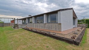 Uma casa moderna térrea com telhado plano, janelas amplas e varanda coberta.