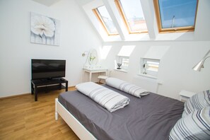 Quarto moderno com cama, televisão, escrivaninha e claraboias.