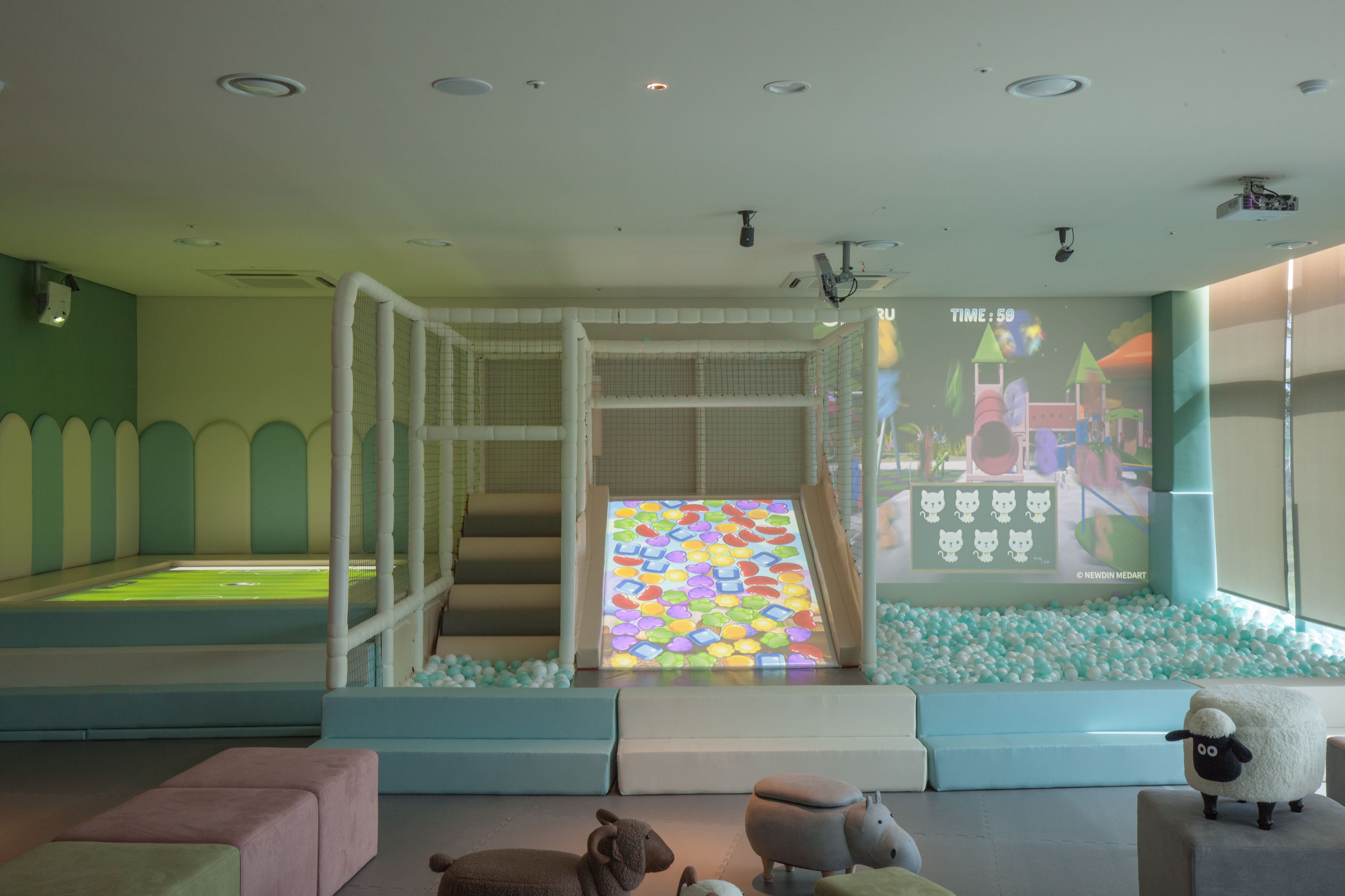 Espaço infantil com escorrega, assentos confortáveis e uma tela de projeção exibindo uma cena colorida.