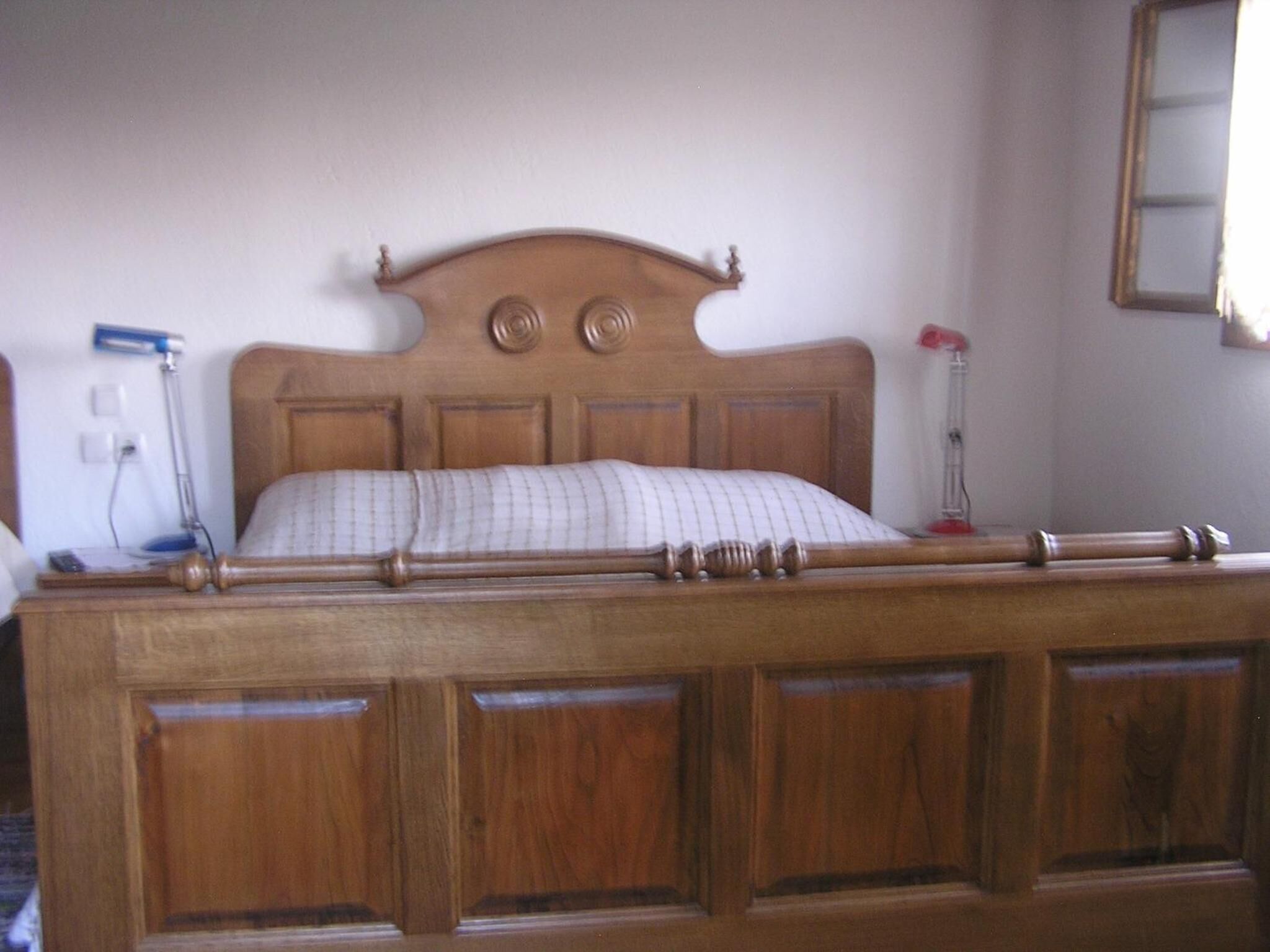 Uma cama de madeira com cabeceira, um abajur e um espelho na parede.