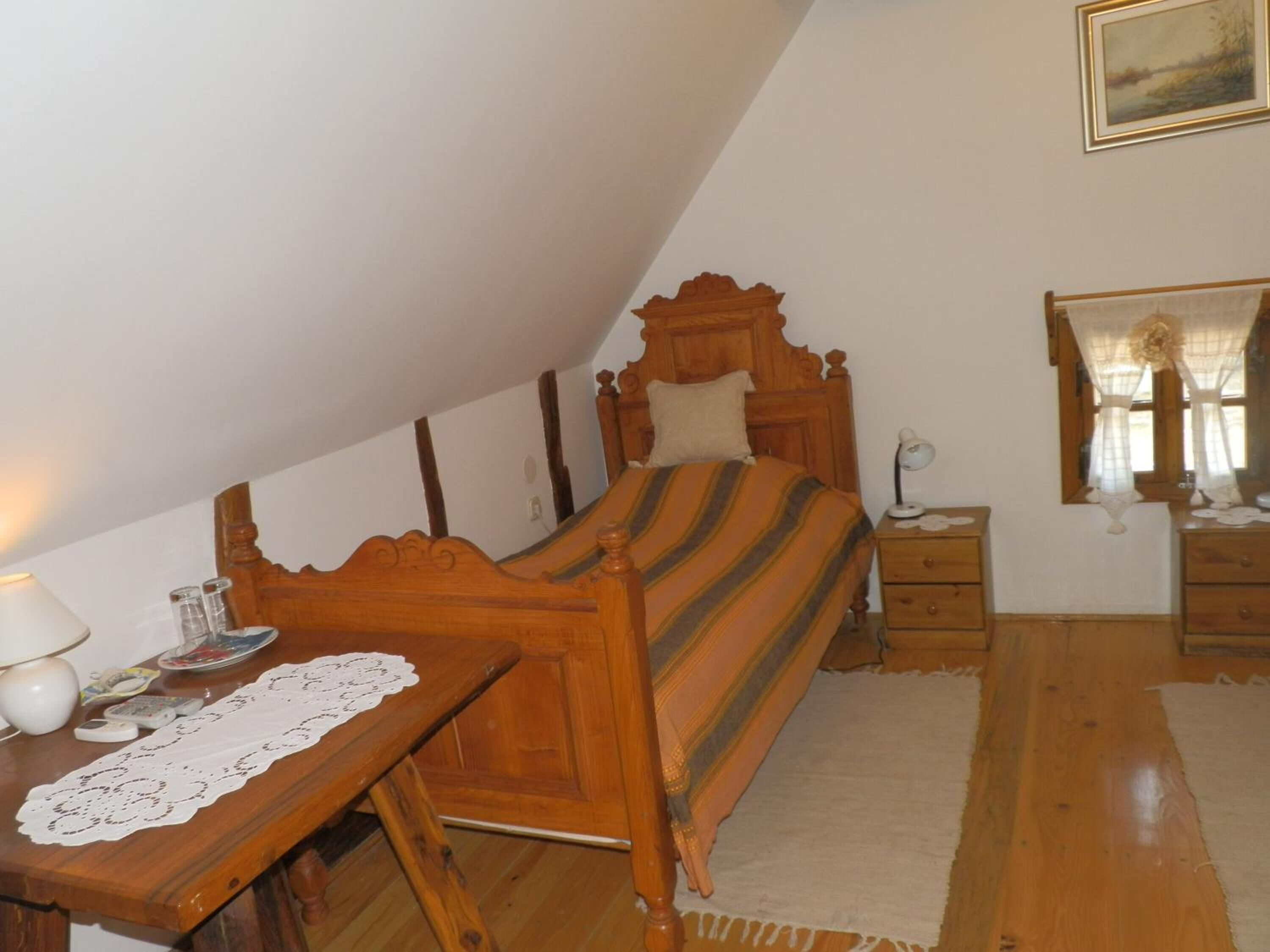 Quarto com cama de madeira, mesa de cabeceira, cômoda e janela com cortinas.