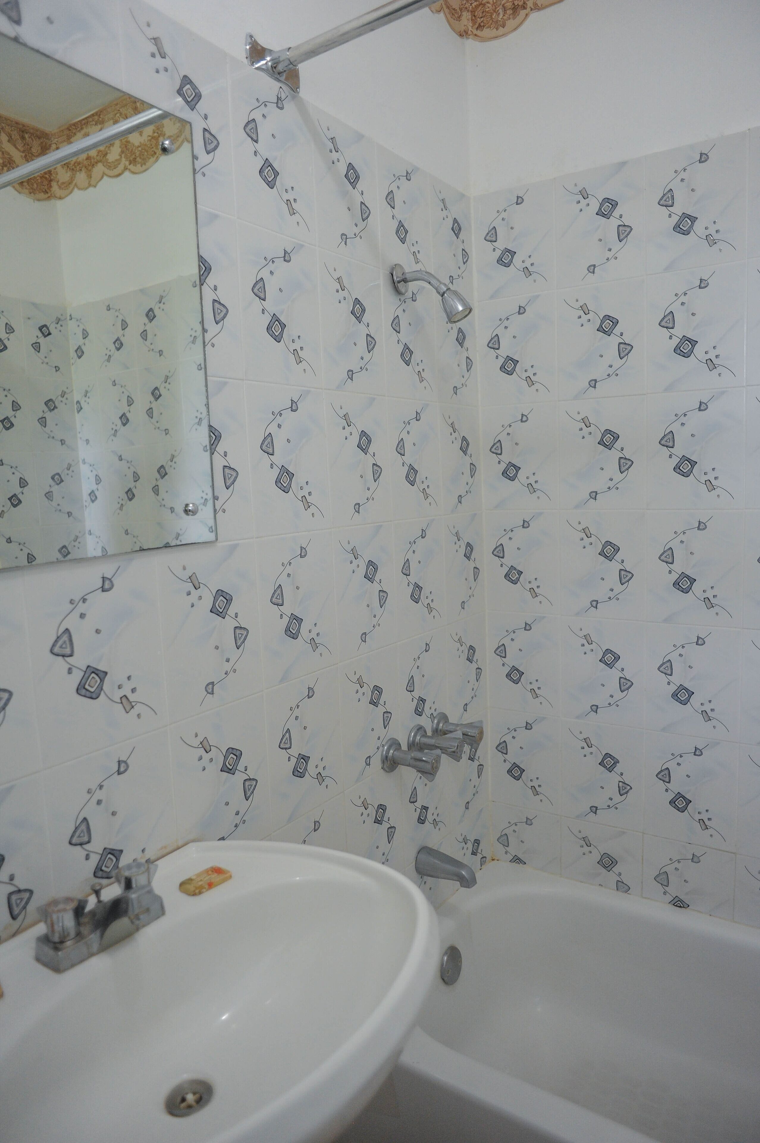 Casa de banho com lavatório, banheira e chuveiro. As paredes exibem um padrão de azulejos geométricos.
