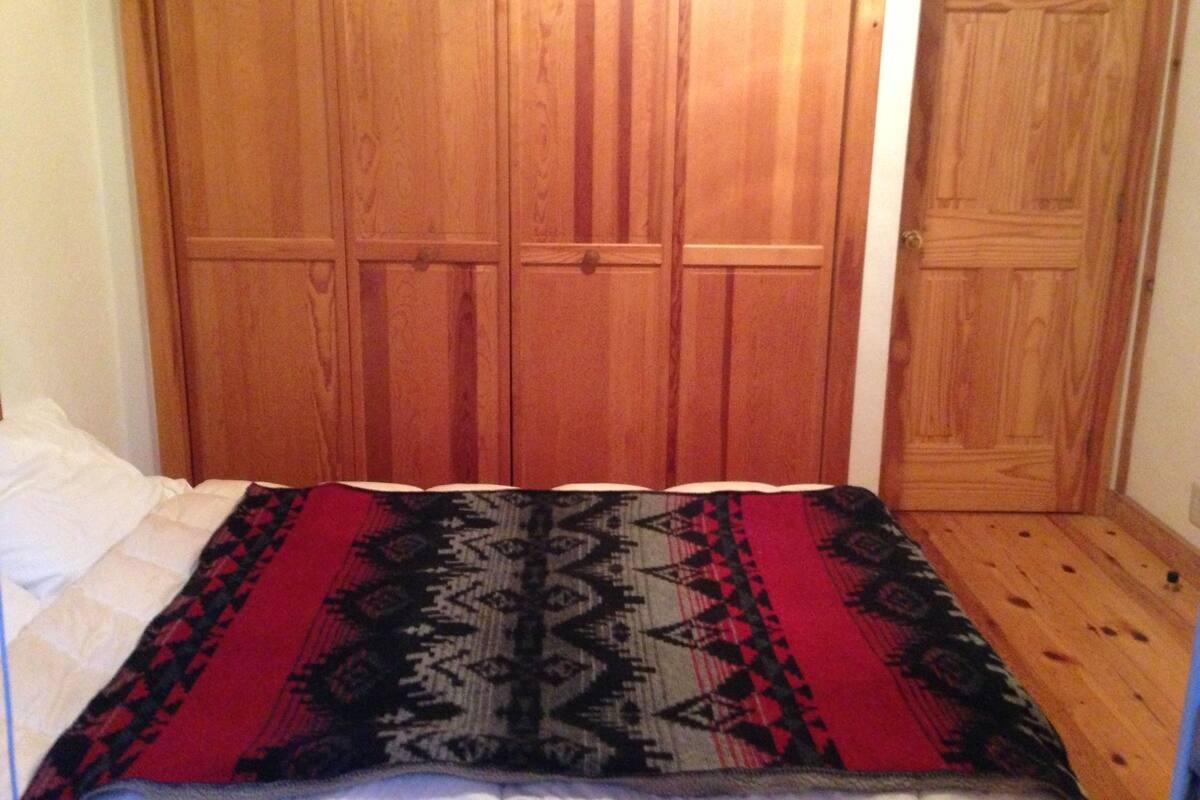 Quarto com cama, manta estampada e armários de madeira.