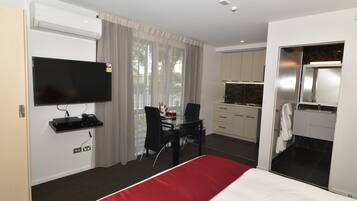 Quarto de hotel com cama, escrivaninha, cadeira, televisão, cozinha compacta e banheiro.