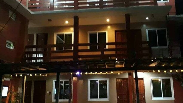 Um edifício de vários andares com varanda no andar superior, área de estar externa e espaço coberto com luzes de corda.