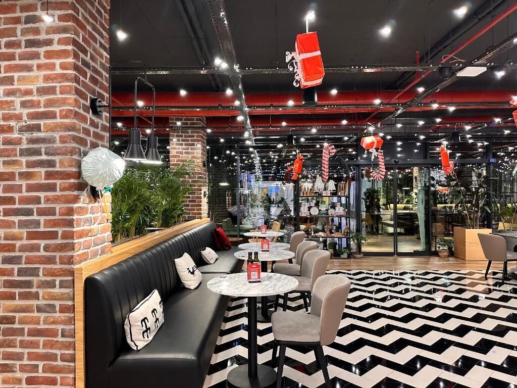 Decoração moderna com parede de tijolos, piso em padrão preto e branco, área de estar e mesas com cadeiras.