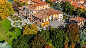 Vista aérea de um complexo histórico com várias estruturas, rodeado por vegetação exuberante e um jardim bem cuidado.