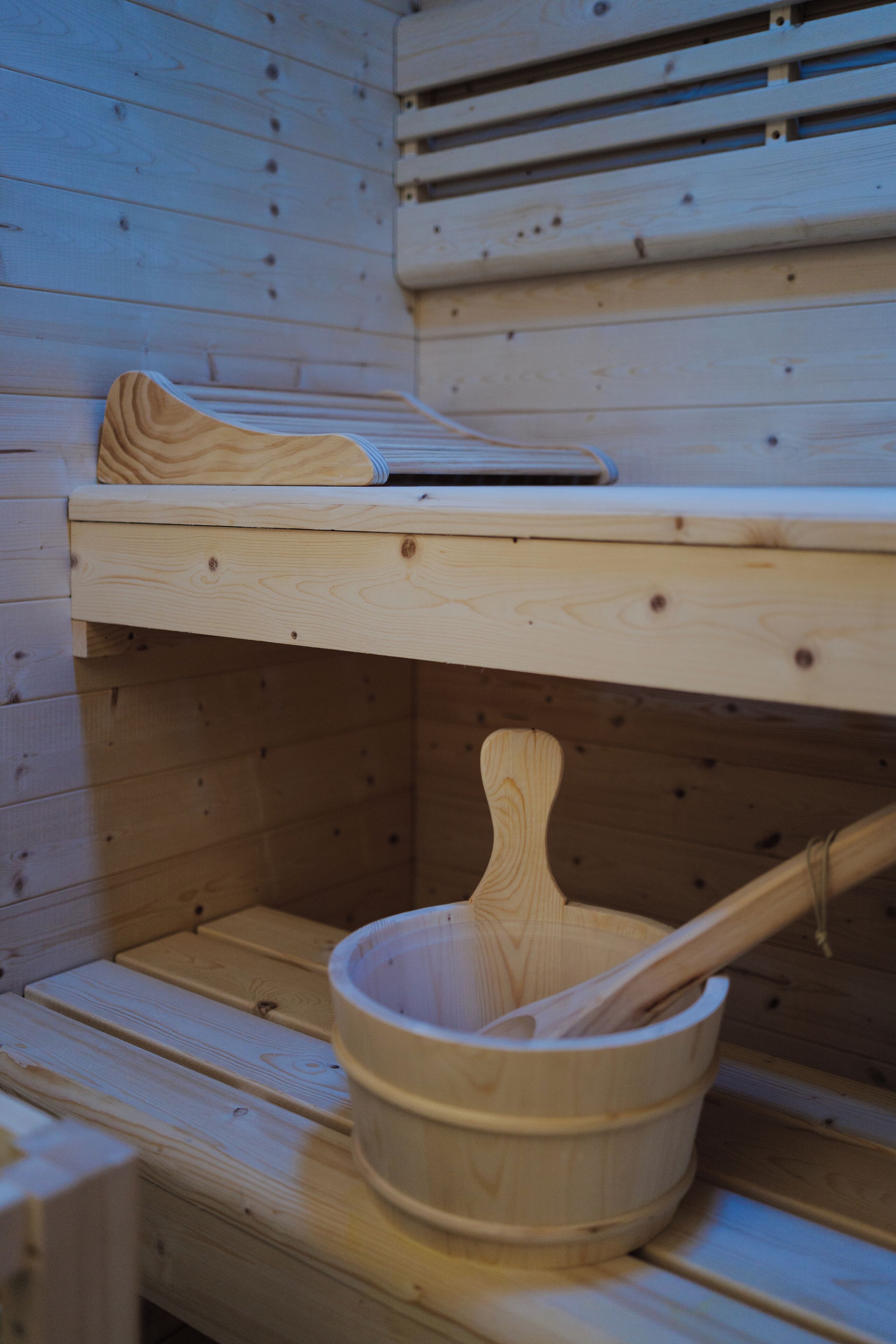 Uma sauna de madeira com um banco de madeira e um balde de madeira com um pilão de madeira.