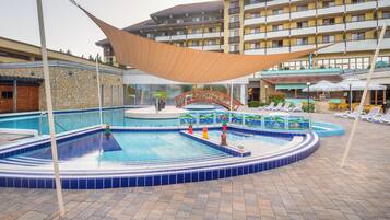 Área de piscina com uma ponte, cadeiras de lounge e um edifício ao fundo.