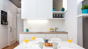 Uma cozinha moderna com armários brancos, bancada com uma tigela de frutas e uma pia. Há dois copos de suco de laranja na mesa de jantar.