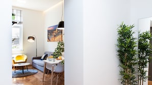 Sala moderna com sofá, mesa de jantar e cadeiras, uma grande planta em vaso e um quadro na parede.