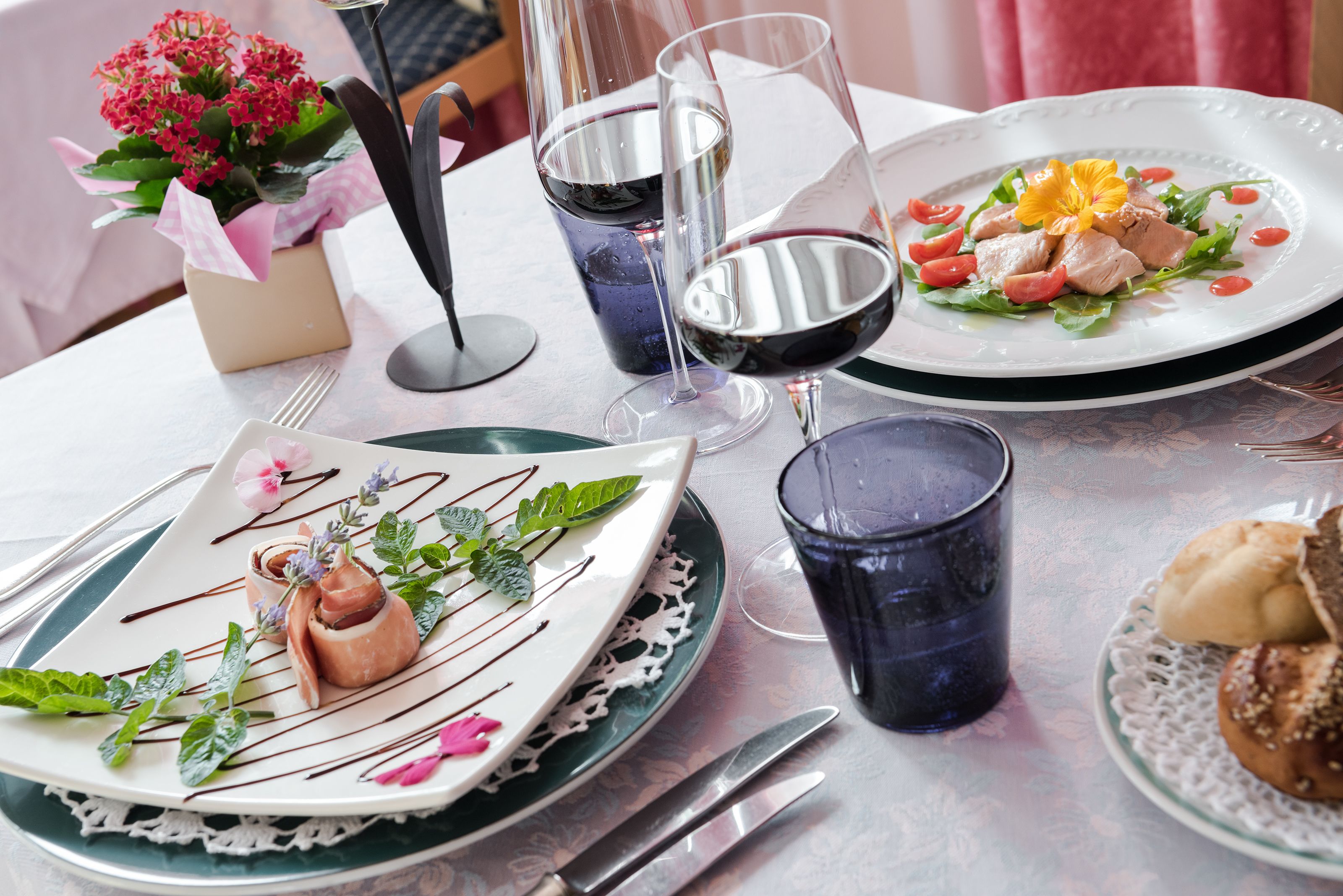 Uma mesa de jantar com pratos de comida, copos de vinho e um vaso de flores.