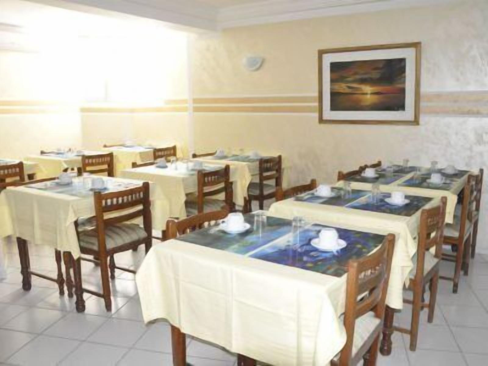 Uma sala de jantar com mesas postas, cadeiras e um quadro na parede.