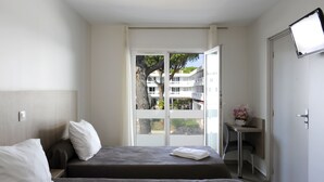 Quarto de hotel com duas camas, uma mesa e vista para um edifício e árvores.