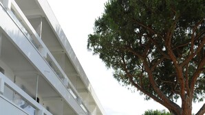 Um edifício moderno com várias varandas e um jardim bem cuidado, com diversas plantas e árvores.