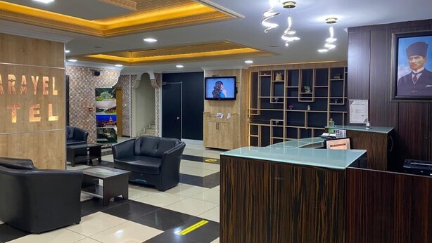 Um saguão de hotel moderno, com balcão de recepção, área de estar e uma tela de televisão.