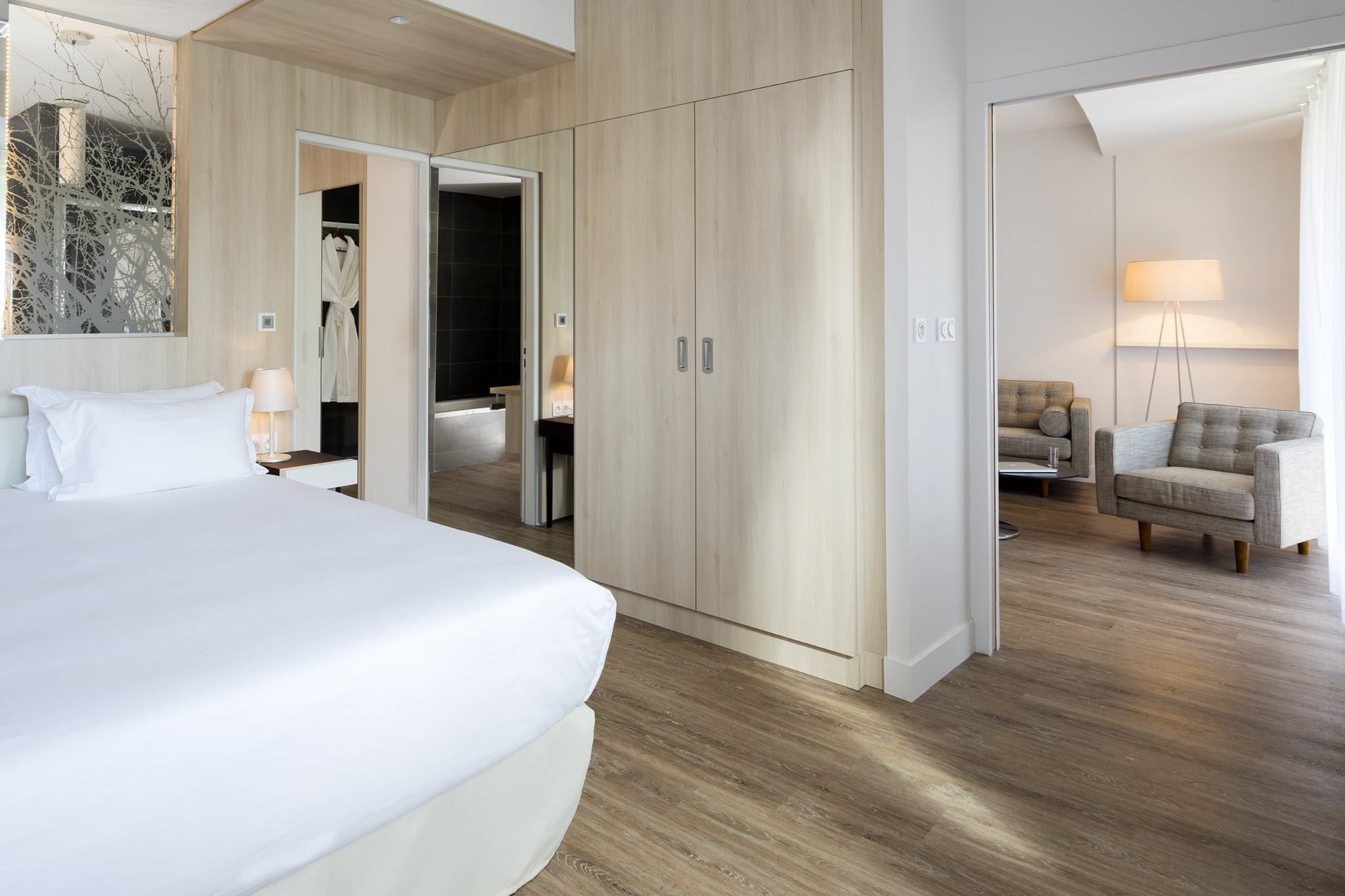 Quarto de hotel moderno com uma cama grande, guarda-roupa de madeira e área de estar com dois sofás.