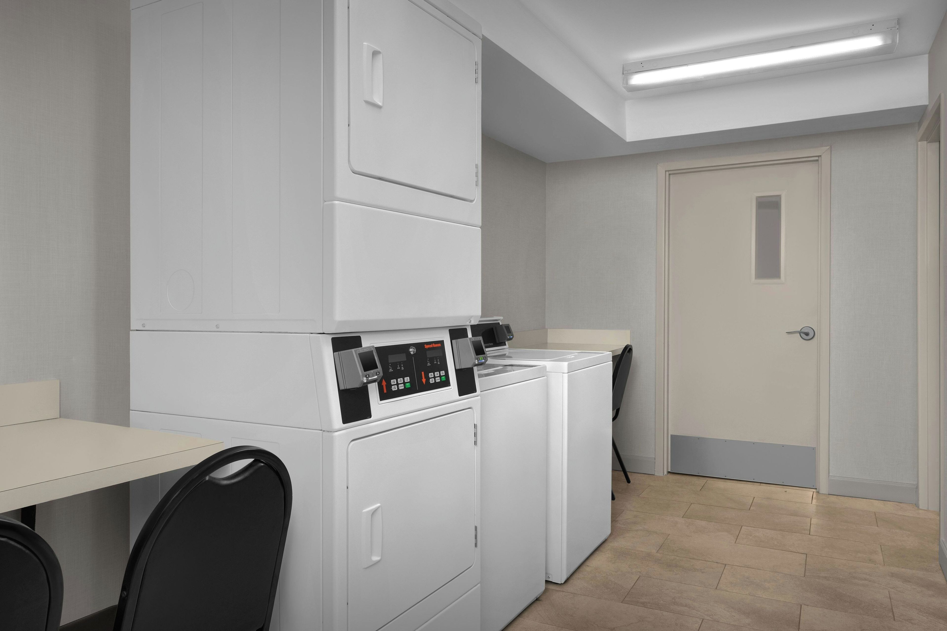 Uma lavanderia com máquinas de lavar e secar empilhadas, um painel de controle e uma porta.