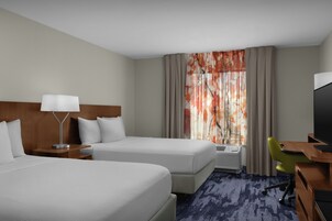 Quarto de hotel com duas camas, uma escrivaninha, uma cadeira, uma televisão e uma janela com cortinas.