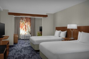 Quarto de hotel com duas camas, uma escrivaninha, televisão e uma luminária.