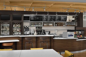 Um espaço de bar moderno com diversas opções de assento, máquina de café e variedade de bebidas e petiscos.