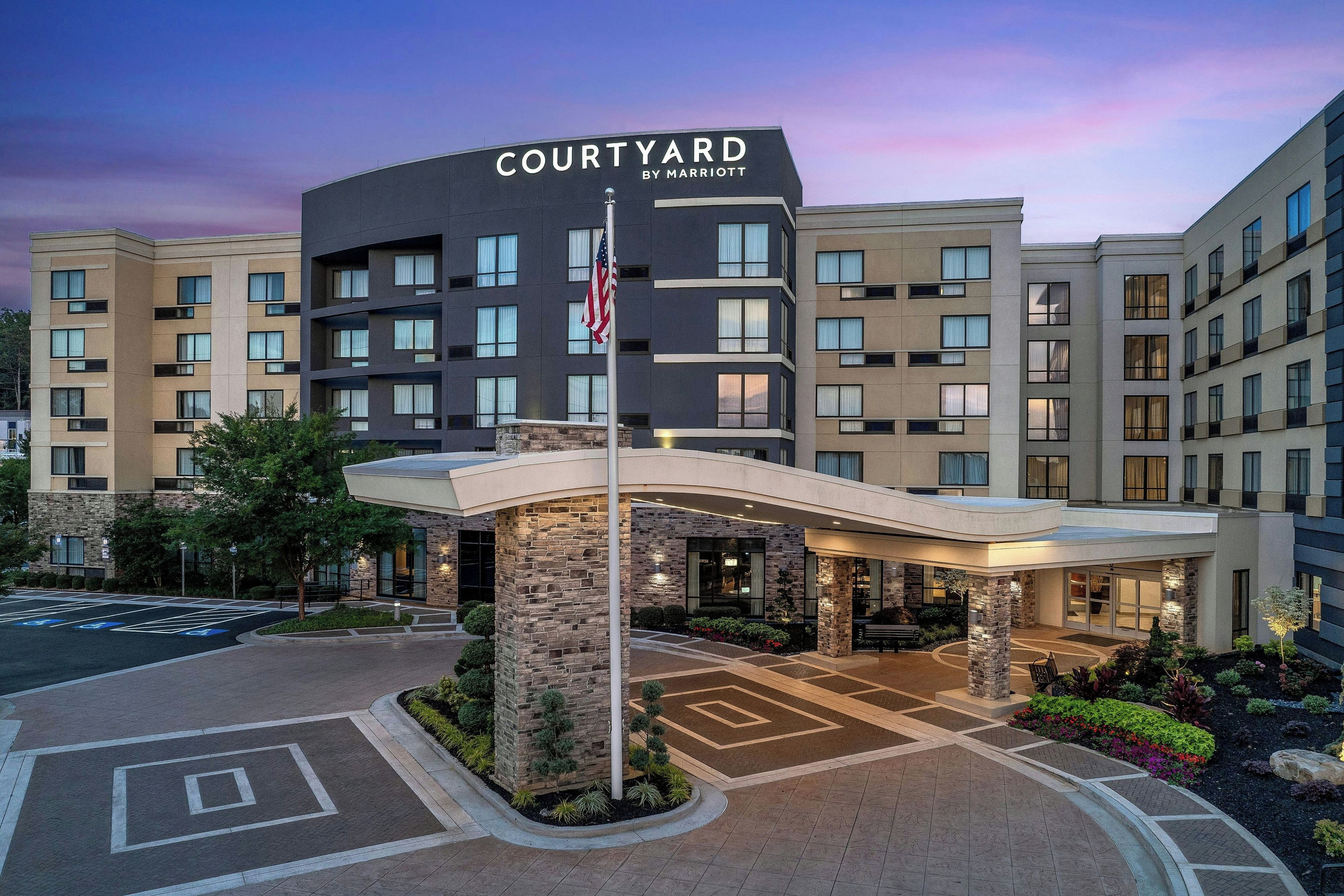 Hotel Courtyard by Marriott com design moderno, apresentando um pátio central com assentos e um mastro.