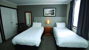 Quarto de hotel com duas camas, mesa de cabeceira com abajur, espelho e quadro na parede.
