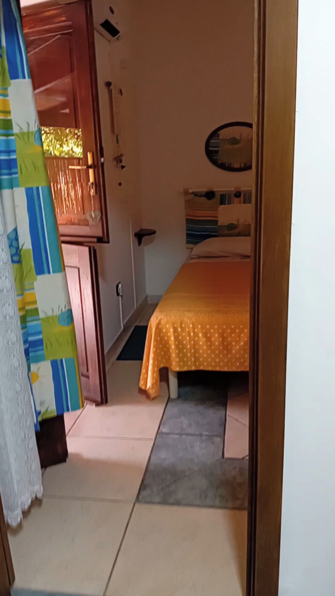 Quarto com cama, mesa de cabeceira, espelho e porta para outro cômodo.