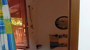 Quarto com cama, mesa de cabeceira, espelho e porta para outro cômodo.