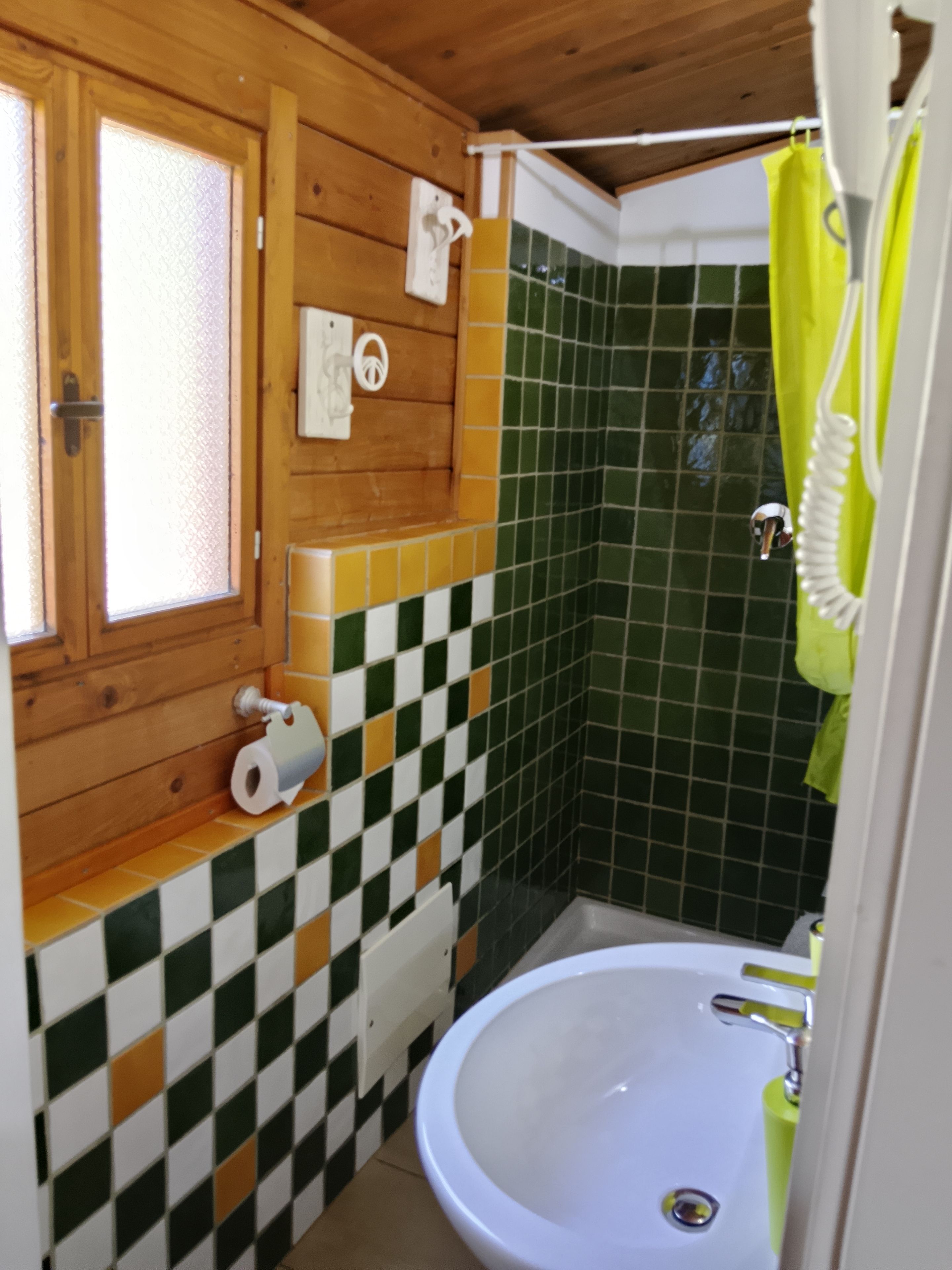 Casa de banho com parede de azulejos quadriculada, lavatório e janela com moldura de madeira.