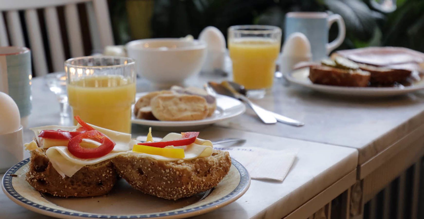 Uma mesa posta para o café da manhã, com torradas cobertas de creme e fruta, um copo de suco de laranja e uma xícara de café.