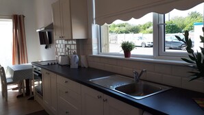 Uma cozinha moderna com armários brancos, bancada preta, pia embutida e janela com vista para a rua.