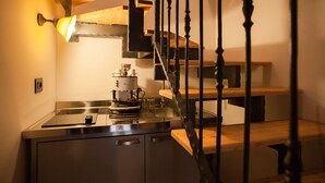 Cozinha com cafeteira, pia e escada de madeira.