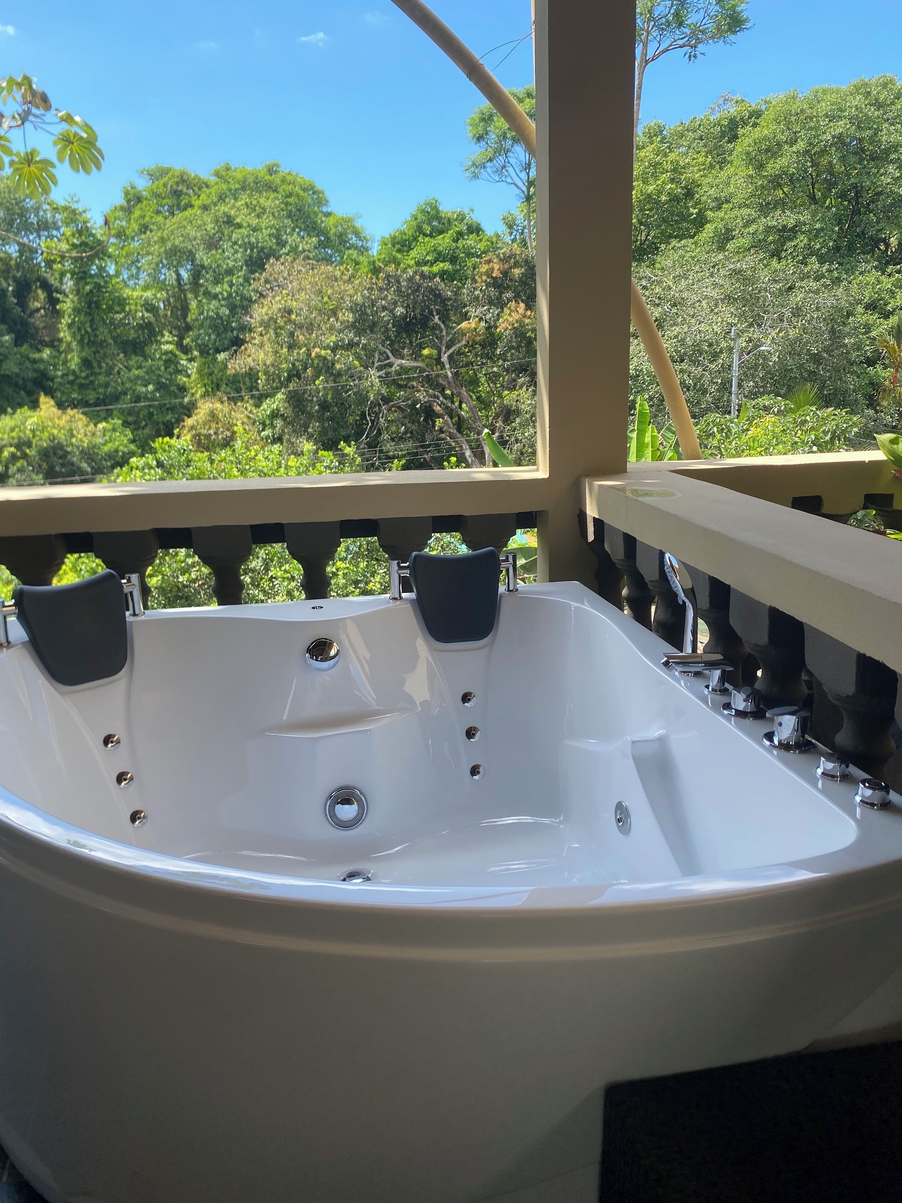 Uma banheira de hidromassagem com vista para vegetação exuberante e um céu azul límpido.
