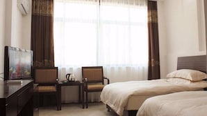 Quarto de hotel com duas camas, uma mesa de trabalho com televisão e uma janela com cortinas.