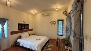 Quarto com cama, mesa de cabeceira, ar condicionado fixado na parede e janela com cortinas.