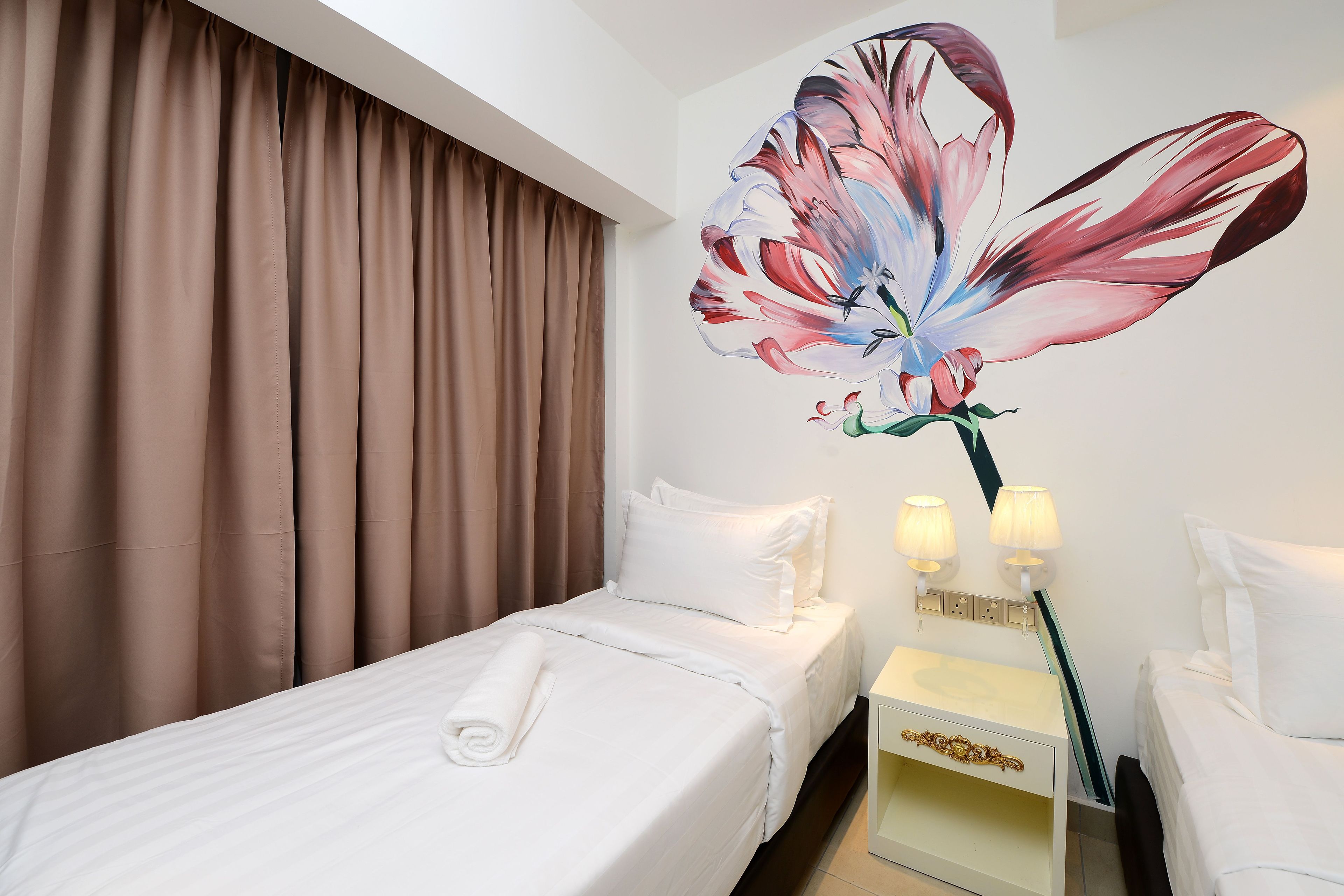 Quarto de hotel com cama, mesa de cabeceira com luminárias e um grande mural floral na parede.