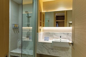 Um banheiro moderno com box de vidro, bancada de mármore e pia.