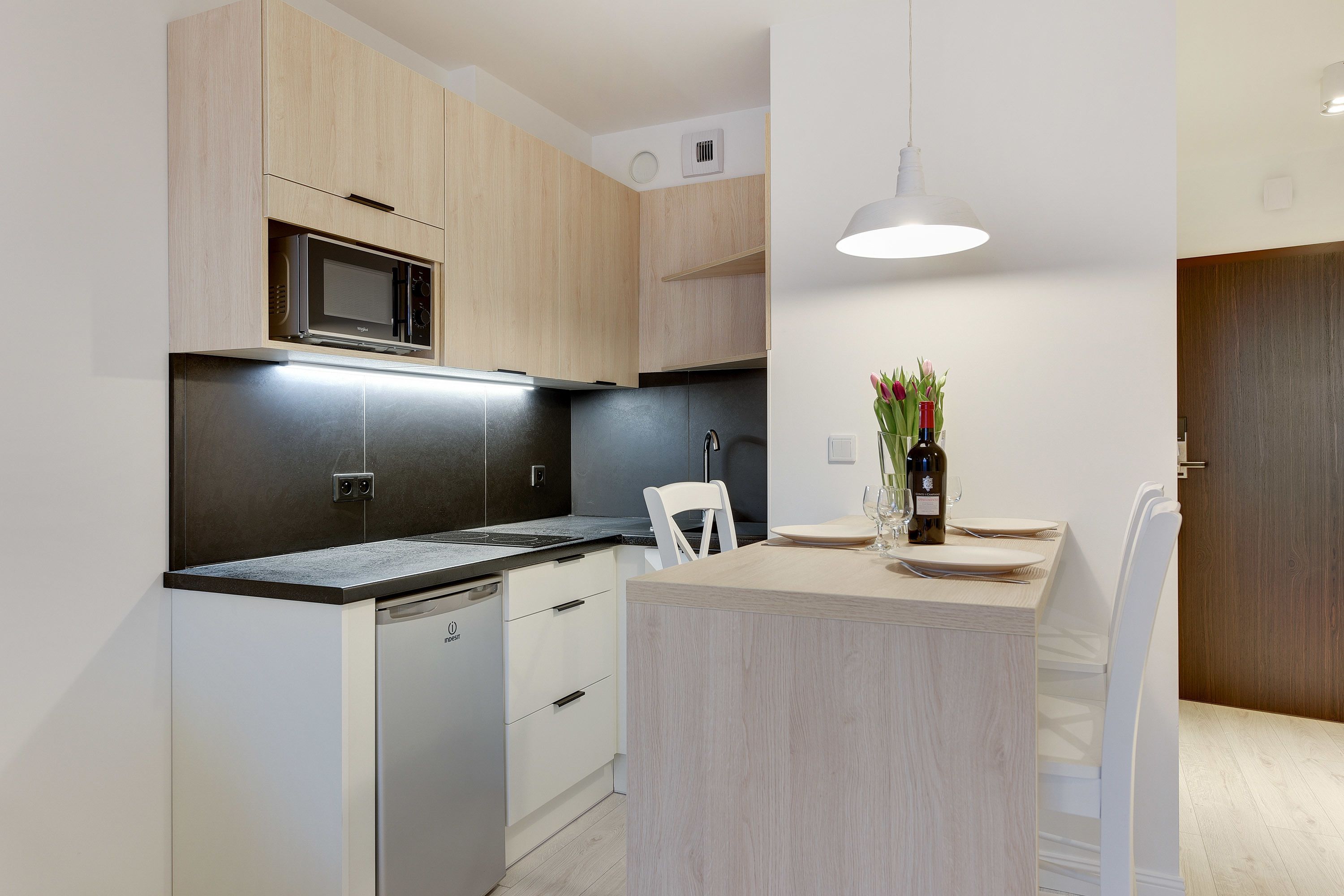 Uma cozinha moderna com micro-ondas embutido, máquina de lavar louça e sala de jantar com mesa e cadeiras.