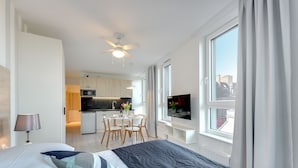 Quarto de hotel moderno com uma cama grande, televisão, área de jantar e vista da cidade.